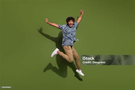 의 전체 길이 사진 감동 펑키 남자가 입고 프린트 셔츠 점프 높은 팔 측면 고립 된 카키 색 배경 20 24세에 대한 스톡 사진