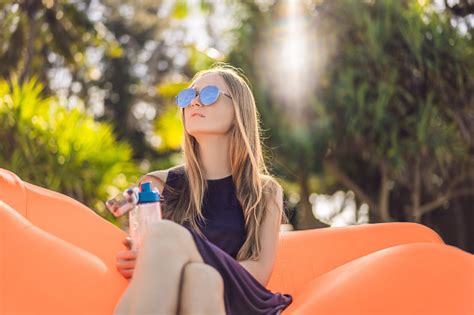 오렌지 풍선 소파에 앉아 열대 섬의 해변에 물을 마시는 예쁜 소녀의 여름 라이프 스타일 초상화 에어 베드에서 편안하고 즐거운 생활 30 34세에 대한 스톡 사진 및 기타