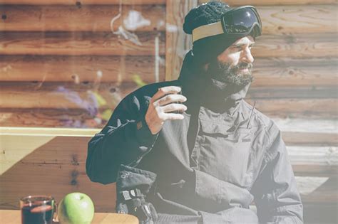 수염 잘생긴 Snowboarded 타고 세션 후 나머지를 복용 햇볕이 잘 드는 테라스에서 따뜻한 차 한잔 마시는 젊은 남자 흐리게 배경입니다 Horizontalvisual