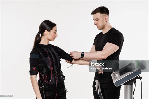 트레이너는 소녀 Ems 슈트를 입고 흰색 배경에서 훈련하기 전에 접촉기를 확인합니다 Ems 전기 충격 근육 자극 슈트에서 스포츠 그룹 훈련 18 19세에 대한 스톡 사진 및