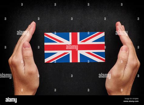 Hands Protecting British Flag On Black Chalkboard Background Close Up