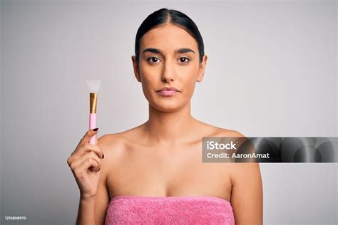 젊은 아름 다운 갈색 머리 여자 착용 수건 샤워 후 적용 화장품 주걱을 사용 하 여 자신감 있는 표정으로 스마트 얼굴 생각 심각한 갈색 머리에 대한 스톡 사진 및 기타