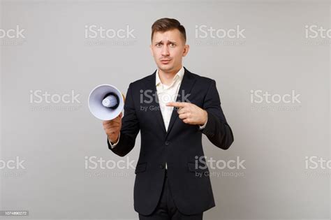 클래식 블랙에 당황한 젊은 사업가 셔츠 스튜디오에 회색 벽 배경에 고립 된 확성기에 포인팅 검지 손가락에 맞게 성과 경력 부 비즈니스 개념입니다 복사 공간을 비웃는 다 검은