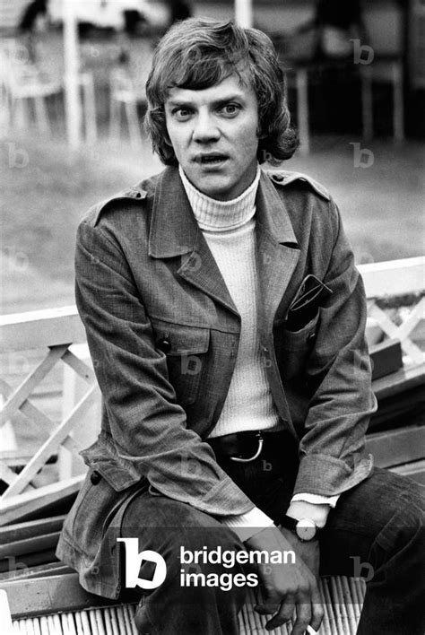 Image Of Malcolm Mcdowell Seated Outside While Talking And Smoking A Cigarette