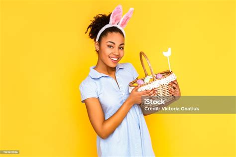 부활절 축 하 개념입니다 젊은 여 자가 귀여운 드레스와 토끼 귀는 노란색에 고립 된 서 있는 계란의 바구니와 함께 카메라 즐거운 갈색 머리에 대한 스톡 사진 및 기타 이미지