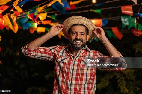 밀짚모자와 체크무늬 셔츠를 입고 브라질 전통 축제 Junina에서 행복한 남자 형형색색의 깃발과 따뜻한 조명이 축제의 밤 배경을 장식합니다 40 44세에 대한 스톡 사진 및