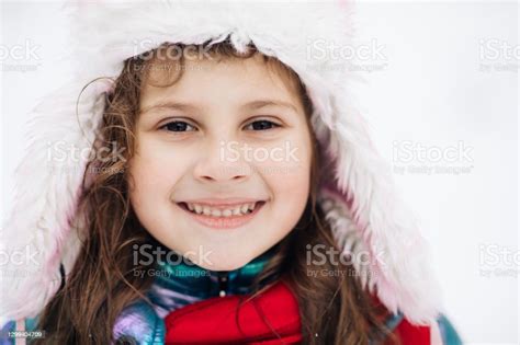 겨울 날에 야외에서 웃고 재미있는 귀여운 소녀 붉은 모자와 스카프에 긴 머리와 미소 예쁜 어린 소녀는 겨울 시간에 흰색 눈 덮인 공원이나 숲에 서 12월에 대한 스톡 사진