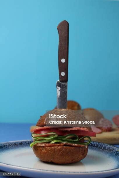 소시지 야채 오이 토마토와 메밀 호밀 빵이 있는 버거 샌드위치가 파란색 배경의 파란색 접시에 놓여 있습니다 세로 사진 체리 토마토는 근처에 놓여 있습니다 패스트 푸드 0명에