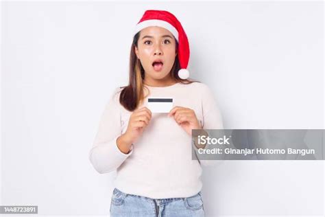 흰색 배경에 격리된 빈 흰색 신용 카드를 보여주는 크리스마스 모자를 쓴 놀란 젊은 아시아 여성 12월에 대한 스톡 사진 및 기타 이미지 Istock