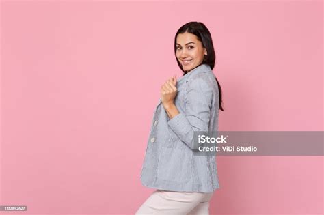 스튜디오에서 분홍색 파스텔 벽 배경에 고립 된 카메라를 찾고 스트라이프 재킷에 손을 잡고 웃는 즐거운 젊은 여자의 측면도 사람들은 진심으로 감정 라이프 스타일 개념입니다