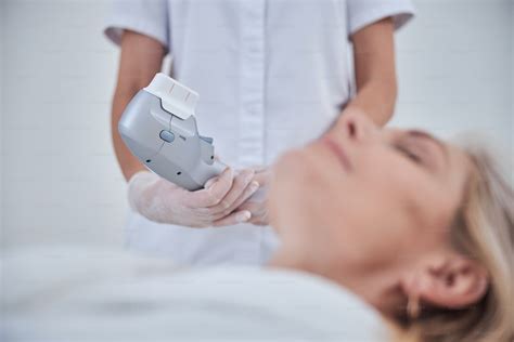 의사가 미용 클리닉의 여성 환자 근처에 서 있는 동안 의사의 손에 현대 초음파 기계의 초상화를 닫습니다 사진