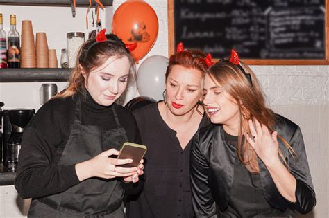 커피 숍 카페에서 할로윈 파티 재미 있고 웃고 재미 있고 놀랐고 할로윈 의상을 입고 휴대 전화 스마트 폰을 보면서 여성 웨이터를 찡그리며 웃고 있습니다 할로윈 빵집 커피 숍