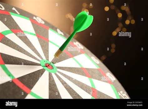 Green Arrow Hitting Target On Dart Board Against Black Background With Blurred Lights Closeup