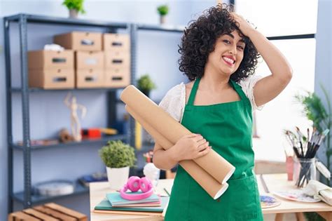 종이 청사진을 들고 곱슬 머리를 가진 젊은 갈색 머리 여자는 머리에 손을 얹고 스트레스를 받고 좌절하고 놀랐고 화난 얼굴로 좌절했다 갈색 머리에 대한 스톡 사진 및 기타