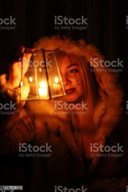 손에 등불을 들고 얼굴에 상징이 새겨진 후드를 입은 마녀 의상을 입은 여성이 카메라를 조심스럽게 바라본다 할로윈을위한 마녀의 이미지 할로윈 축하의 개념 가로등에 대한 스톡