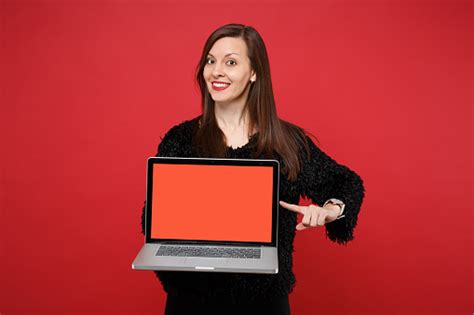 노트북 Pc 컴퓨터 빨간색 배경에 고립 된 빈 빈 화면에 검은 모피 스웨터 포인팅 검지 손가락에 아주 젊은 여자 사람들이 진심으 감정 라이프 스타일 개념 복사 공간을 비웃는