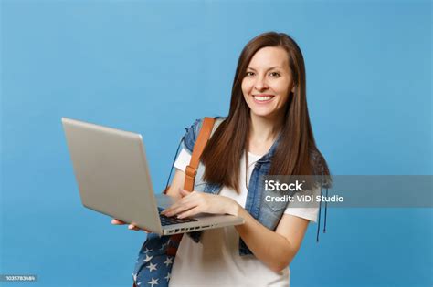 배낭 들고와 작업을 사용 하 여 노트북 Pc 컴퓨터 파란색 배경에 고립에 데님 옷에서 젊은 매력적인 행복 한 여자 학생 대학에서