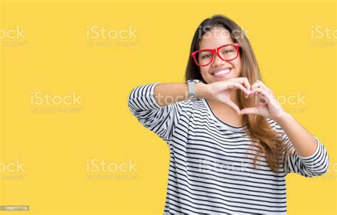 젊은 아름 다운 갈색 머리 여자 안경을 줄무늬 스웨터와 레드 심장 기호와 손으로 모양을 보여주는 사랑에 웃 고 고립 된 배경 위에 낭만적인 개념입니다 갈색 머리에 대한 스톡