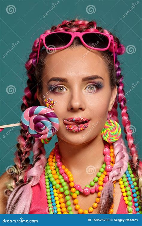 Прекрасная девушка с многоцветными косичками в стиле волос и ярким макияжом позирующая в студии