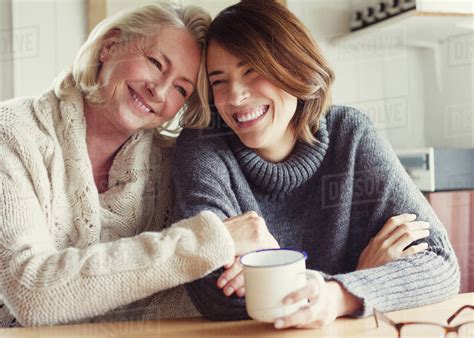 Laughing Mother And Daughter In Sweaters Hugging And Drinking Coffee