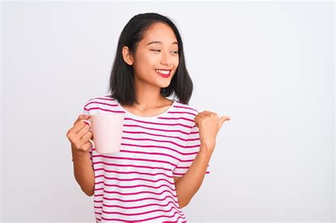 젊은 아름다운 중국 여자 마시는 컵 의 커피 위에 고립 된 흰색 배경 가리키는 과 보여주는 엄지 손가락으로 옆구리 와 행복한 얼굴 미소 가리키기에 대한 스톡 사진 및 기타