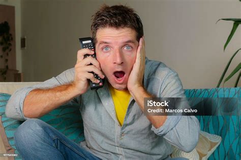 매력적인 영 놀라게 하 고 불신에 깜짝 Tv 뉴스 또는 원격 제어를 들고 거실 소파 소파에서 영화를 보고 연 입으로 캐주얼 옷 집에서 남자 충격 감정에 대한 스톡 사진 및