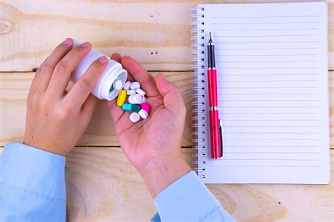 나무 테이블에 책과 펜으로 약을 복용에 흰색 병 알약을 들고 여자 손의 상단보기 열심히 일하고 스트레스가 많은 업무 초과 근무 건강 관리 개념 개념에 대한 스톡 사진 및