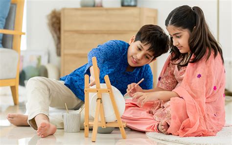 두 사람 인도 형제 자매는 전통적인 옷을 입고 함께 놀고 행복과 함께 접시에 붓 페인팅 아트를 사용하고 집에있는 거실의 바닥에 앉아있었습니다 가족 교육 개념 놀기에 대한