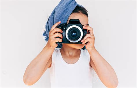 흰색 배경에 고립 된 사진 카메라를 들고 머리에 파란색 터번을 입은 어린 소녀 흰색 배경에 대한 전문 카메라와 함께 사진을 찍는 사랑스러운 아이 건강한 생활방식에 대한 스톡