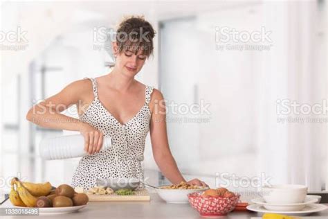 시리얼과 과일과 함께 맛있는 아침 식사를 위해 그릇에 우유를 붓는 미소 짓는 젊은 여성 한 명의 여자만에 대한 스톡 사진 및