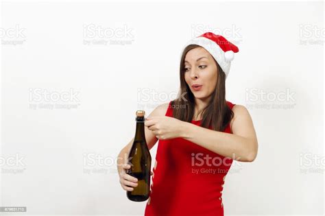 아름 다운 재미 있는 백인 젊은 행복 한 여자 빨간 드레스와 흰색 바탕에 샴페인 병을 열고 하려고 하는 크리스마스 모자에 매력적인 미소로 산타 소녀 격리입니다 새 해 휴일
