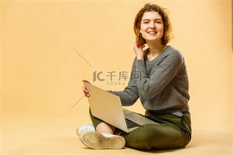 快乐的年轻女人双腿交叉坐在地板上，使用米色背景的笔记本电脑。高清摄影大图 千库网
