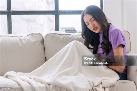불행한 아시아 여성은 집에서 소파에 앉아있는 문제나 생리통을 걱정합니다 몸이 좋지 않은 어린 소녀 아픈 복통 생리통 배꼽 건강에 해로운 질병 월경은 소파에 앉아 있습니다