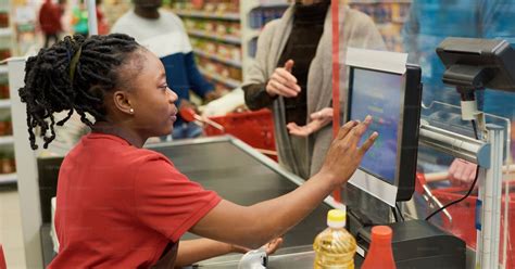 출납원 카운터에서 구매자에게 서비스를 제공하는 동안 식품 가격과 함께 제복을 입은 젊은 흑인 여성의 측면 모습 사진 Unsplash의 조수 이미지