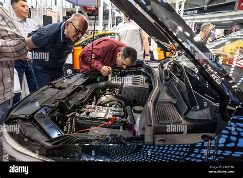 Potential buyers closely inspecting the engine of a brand new car at a car show. The image ...