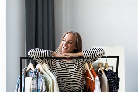 목욕 가운을 입은 귀여운 젊은 여성이 옷걸이 선반 앞에 서서 직장이나 산책을 위해 옷을 입으려고 노력합니다 20 24세에 대한 스톡 사진 및 기타 이미지 Istock