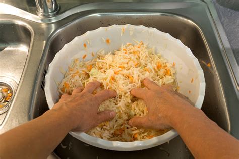 겨울을위한 수제 소금에 절인 양배추 준비 여자의 손은 부엌의 금속 싱크대에있는 플라스틱 대야에 잘게 썬 양배추와 당근을 소금과 함께 반죽하고 섞습니다 실제 사진 Stomp에