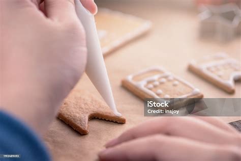 여자는 나무 테이블 배경에 흰색 프로스팅 아이싱 크림 토핑 부엌에서 베이킹 종이 클로즈업 매크로와 진저 브레드 쿠키 하우스를 장식하고 있습니다 가정 주방에 대한 스톡 사진