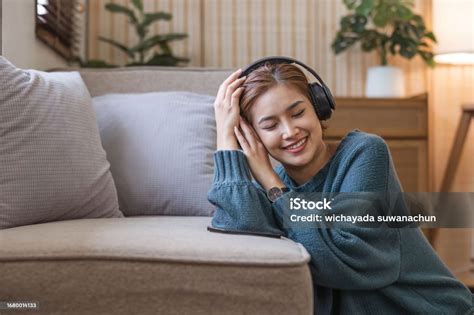 집에서 소파 근처에 앉아 휴대폰으로 음악을 듣는 행복한 아시아 여성 아침에 헤드폰을 끼고 휴식을 취하는 웃는 소녀 휴식을 취할 시간 복사 공간 Brand Name Smart