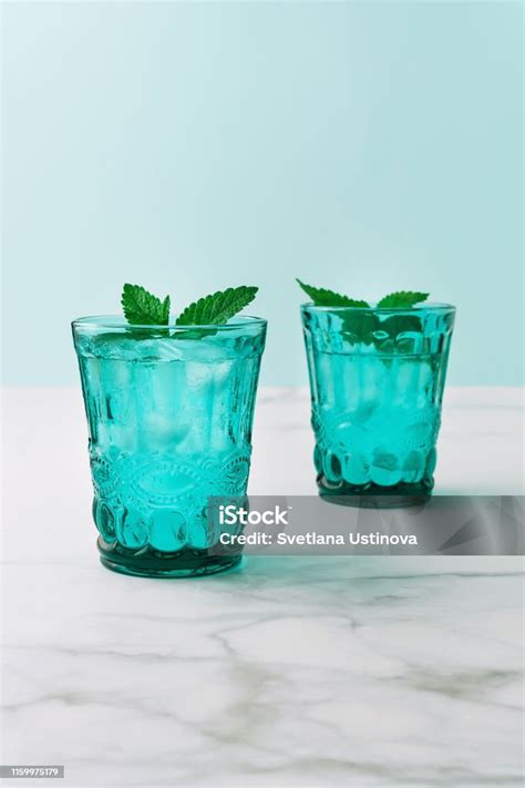 차가운 음료와 얼음 조각이있는 두 개의 아름다운 빈티지 청록색 안경 흰색 대리석 테이블에 신선한 녹색 민트 잎으로 장식 0명에