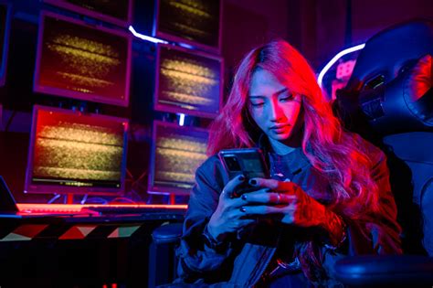 Asian Woman In Front Of A Computer Monitor Display Using Mobile Phone Neon Light Hacker Wear