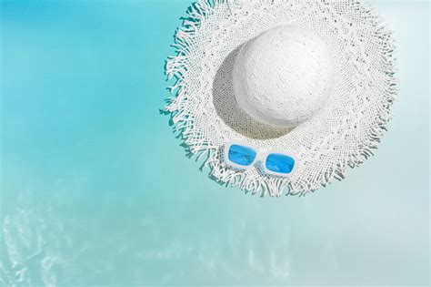 여름 하얀 태양 모자와 색색의 선글라스가 햇빛이 비치는 눈부심 흐릿한 파란색 배경에 바다 파도처럼 햇빛이 비치고 공간을 복사합니다 라이프 스타일 여름 휴가 컨셉 사진 미니멀