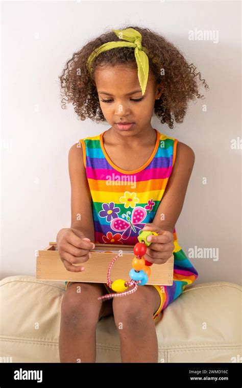Focused Mixed Race Girl Threading Beads Wearing A Colorful Dress With