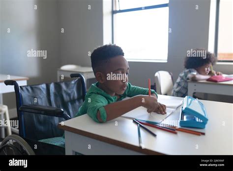 Un Garçon élémentaire Afro Américain écrit Sur Un Livre Tout En étant Assis En Fauteuil Roulant