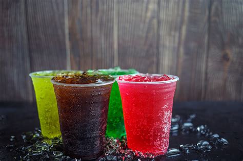 다채롭고 향긋한 플라스틱 잔에 담긴 청량음료와 얼음 조각 검은색 배경에 얼음 위에 차갑게 식힌 청량음료 얼음 위에 청량음료 또는 탄산음료가 있다 가득 찬에 대한 스톡 사진