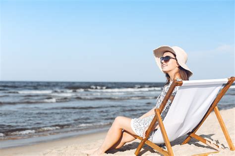 선글라스와 모자를 쓰고 바다 해변의 나무 갑판 의자에서 휴식을 취하는 행복한 갈색 머리 여자 25 29세에 대한 스톡 사진 및 기타 이미지 Istock