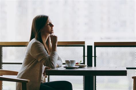 Wanita Muda Yang Menarik Duduk Sendirian Di Dekat Jendela Besar Di ...