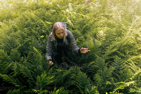 teenage girl sneaks between ferns in a shady forest among ferns