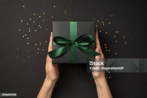 고립된 검은 색 배경에 녹색 리본 활과 황금 색종이가 달린 검은 선물 상자를 들고 있는 여성 손의 1인칭 탑 뷰 사진 녹색에 대한 스톡 사진 및 기타 이미지 Istock