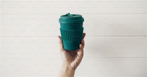 흰색 나무 배경에 세련된 재사용 가능한 에코 커피 컵을 들고 있습니다 천연 대나무 섬유로 만든 그린 컵 제로 웨이스트 개념 일회용 플라스틱을 금지합니다 선택하십시오